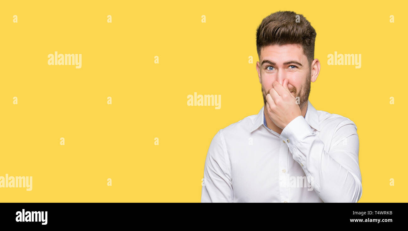 Young handsome business man smelling something stinky and disgusting ...
