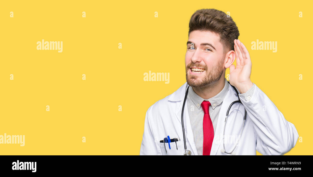 Young handsome doctor man wearing medical coat smiling with hand over ...