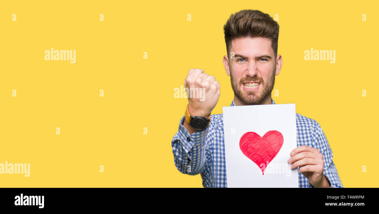 Young handsome man holding paper with red heart annoyed and frustrated ...