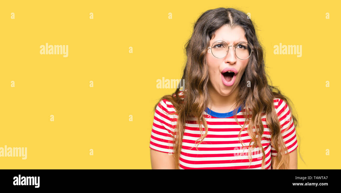 Young beautiful woman wearing glasses In shock face, looking skeptical ...