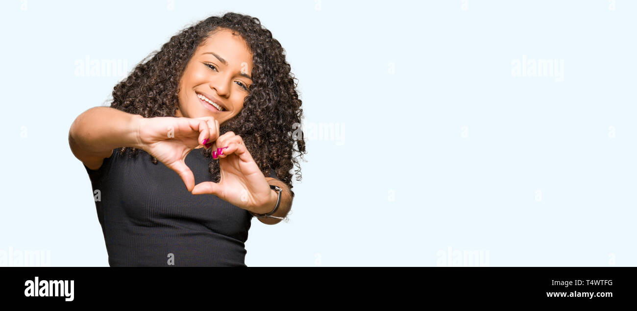 Young beautiful woman with curly hair smiling in love showing heart ...