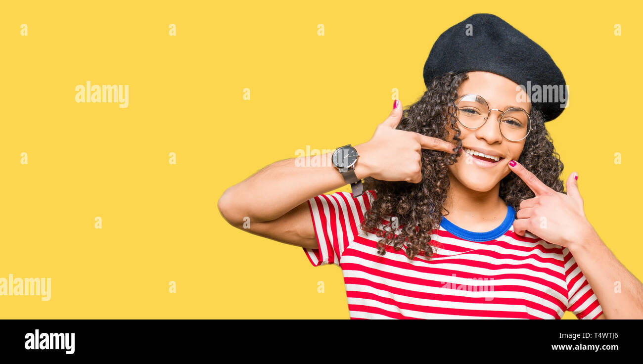 Young beautiful woman with curly hair wearing glasses and fashion beret ...