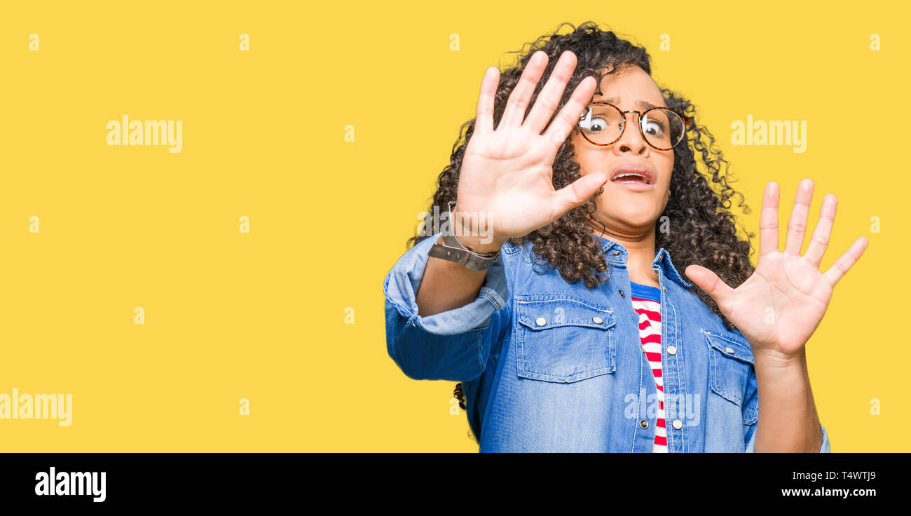 Young beautiful woman with curly hair wearing glasses afraid and ...