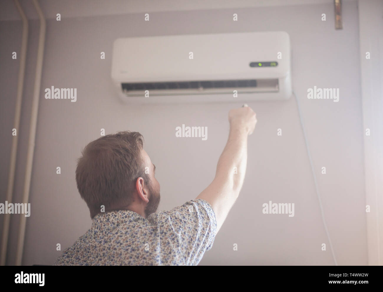 one young man, 20-29 years old, turning on his air conditioner. rear ...