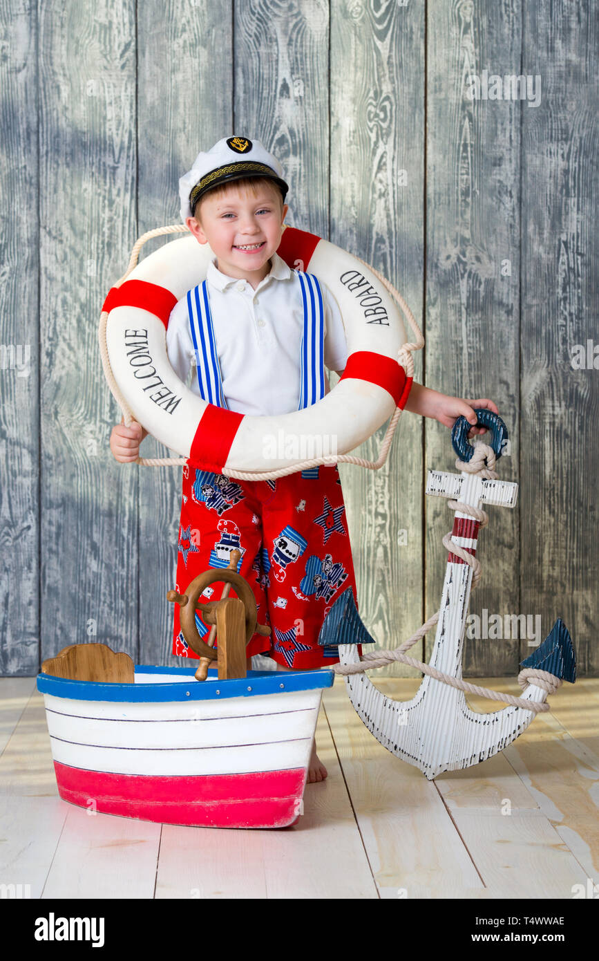 Smiling boy in captain's cap sitting on suitcases and holds in his ...