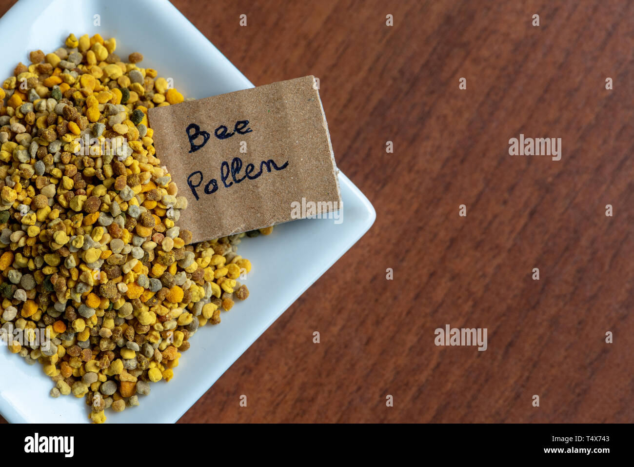 square saucer full of bee pollen with a little tag, on a dark wooden ...