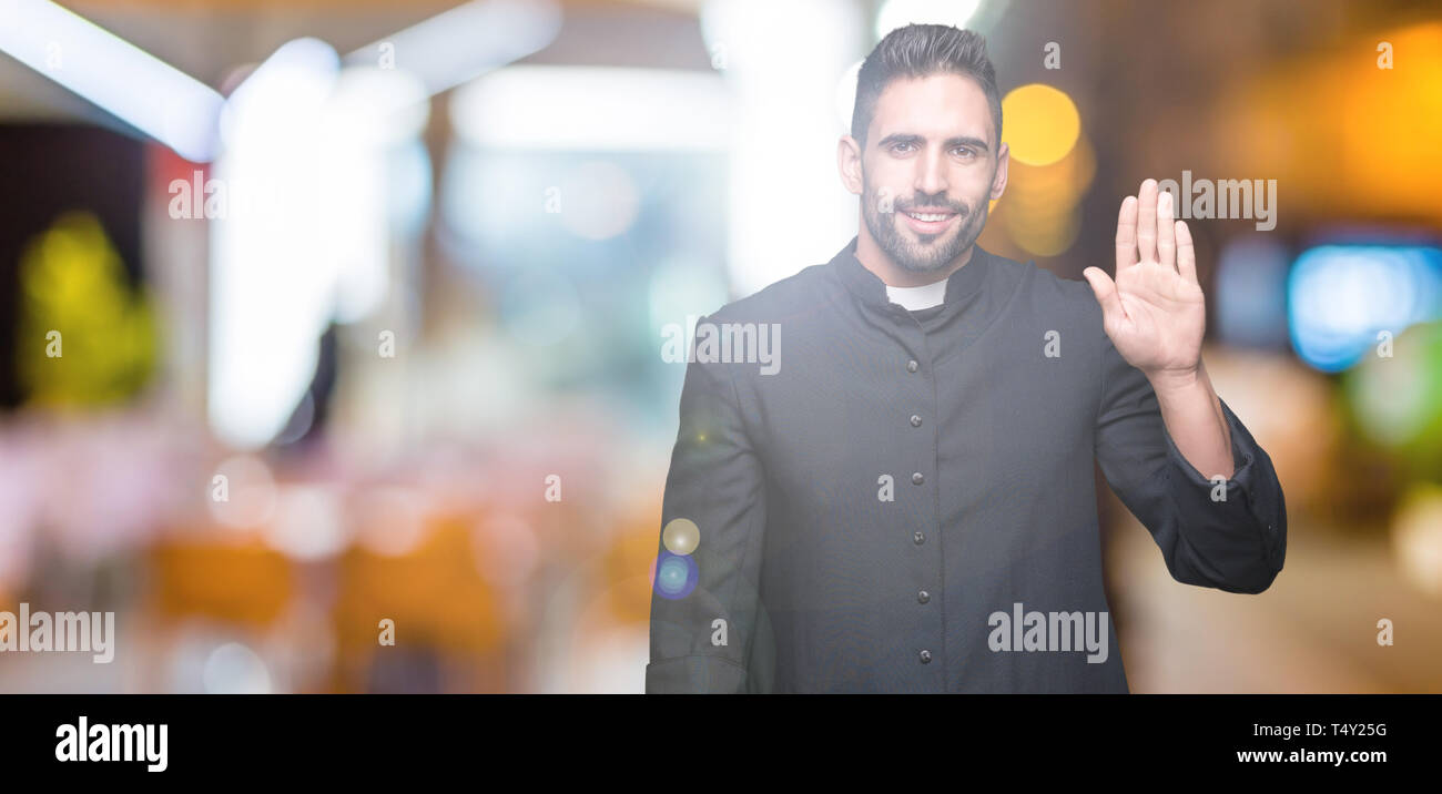 Young Christian priest over isolated background Waiving saying hello ...