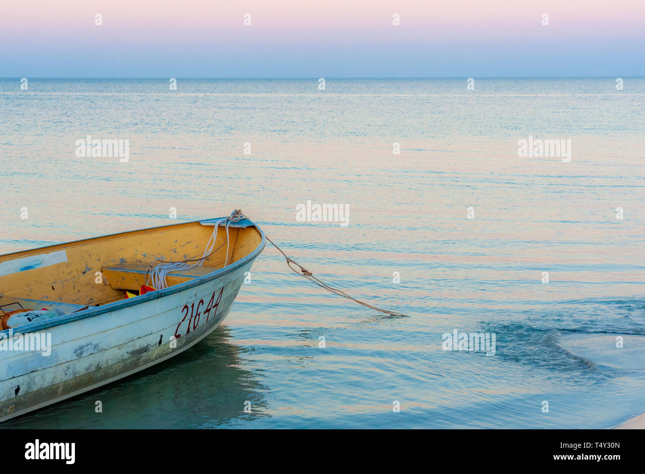 A small dingy or tinny moored at the beach at dusk with waves lapping ...