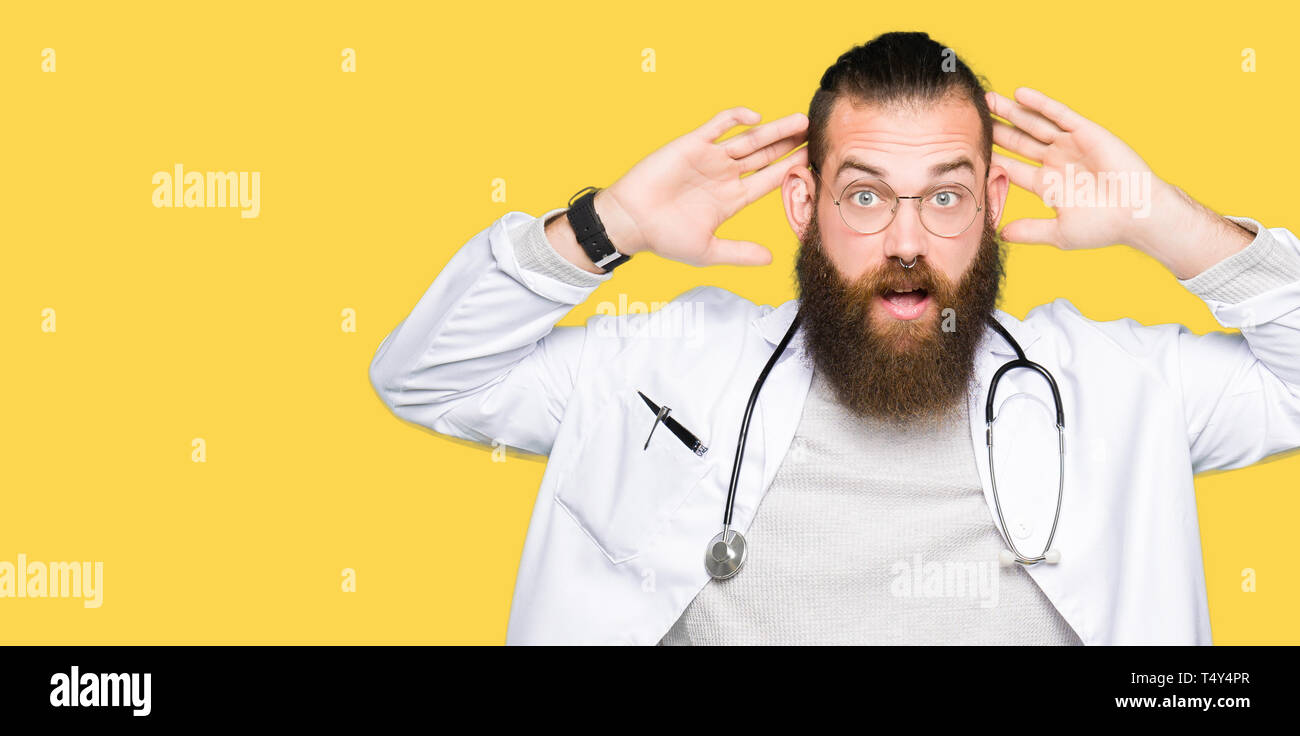 Young blond doctor man with beard wearing medical coat Crazy and scared ...
