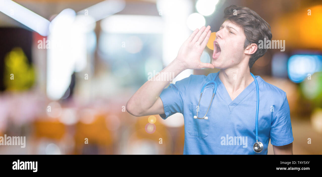Young doctor wearing medical uniform over isolated background shouting ...