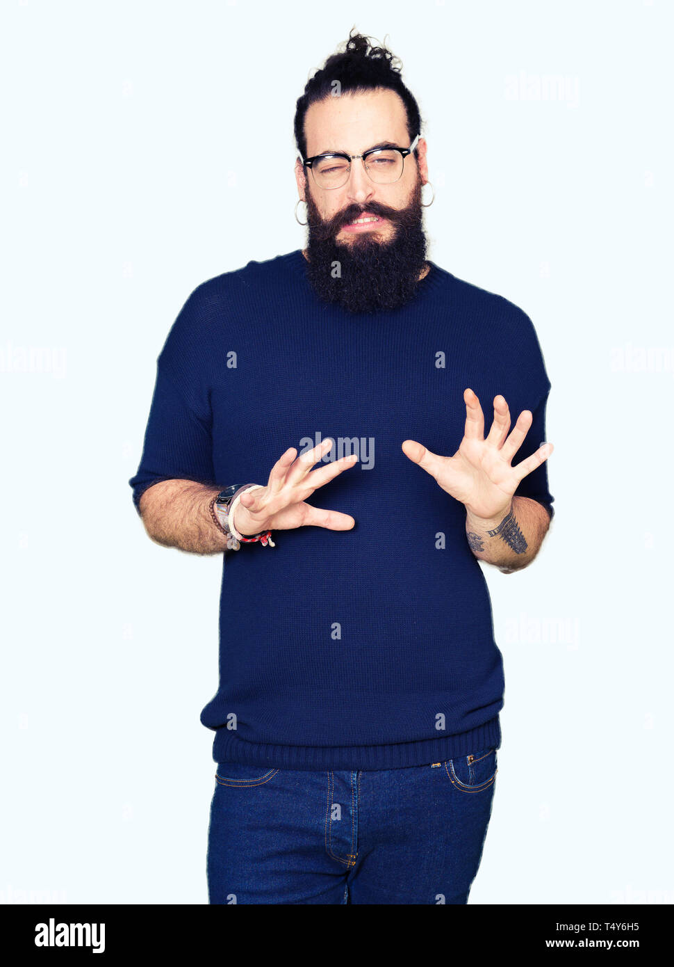 Young hipster man with long hair and beard wearing glasses disgusted ...