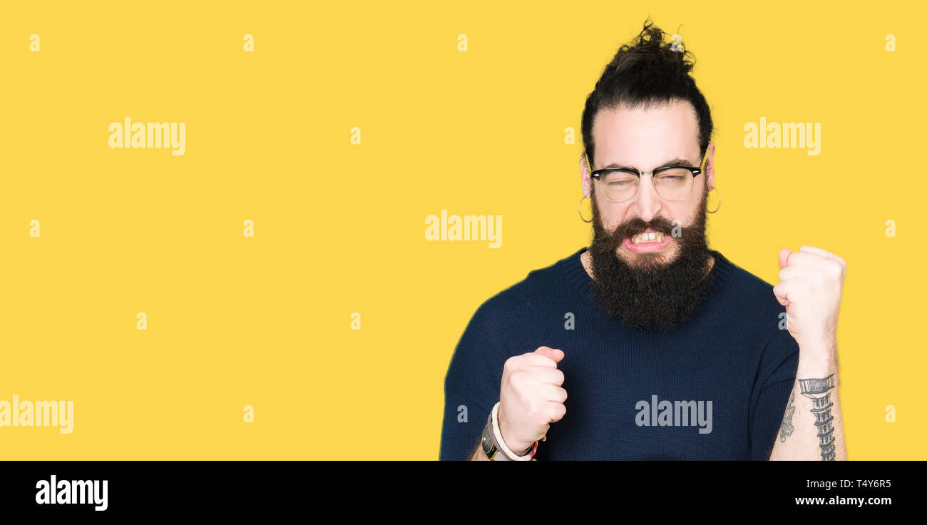 Young hipster man with long hair and beard wearing glasses angry and ...