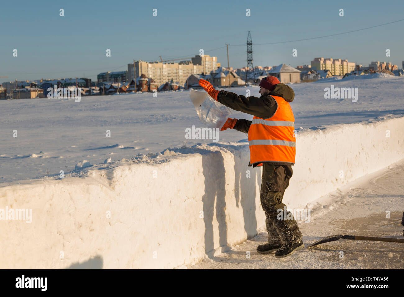 A worker in an orange reflective vest throws an ice block over a snow ...