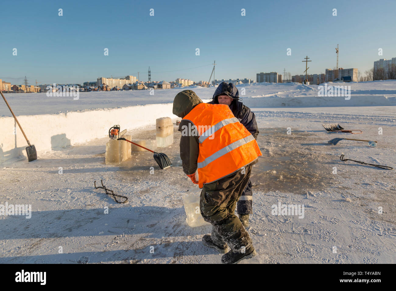 Workers in winter overalls carry an ice block from the hole in their ...