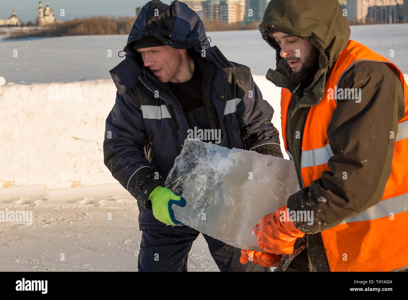 Workers in winter overalls carry an ice block from the hole in their ...