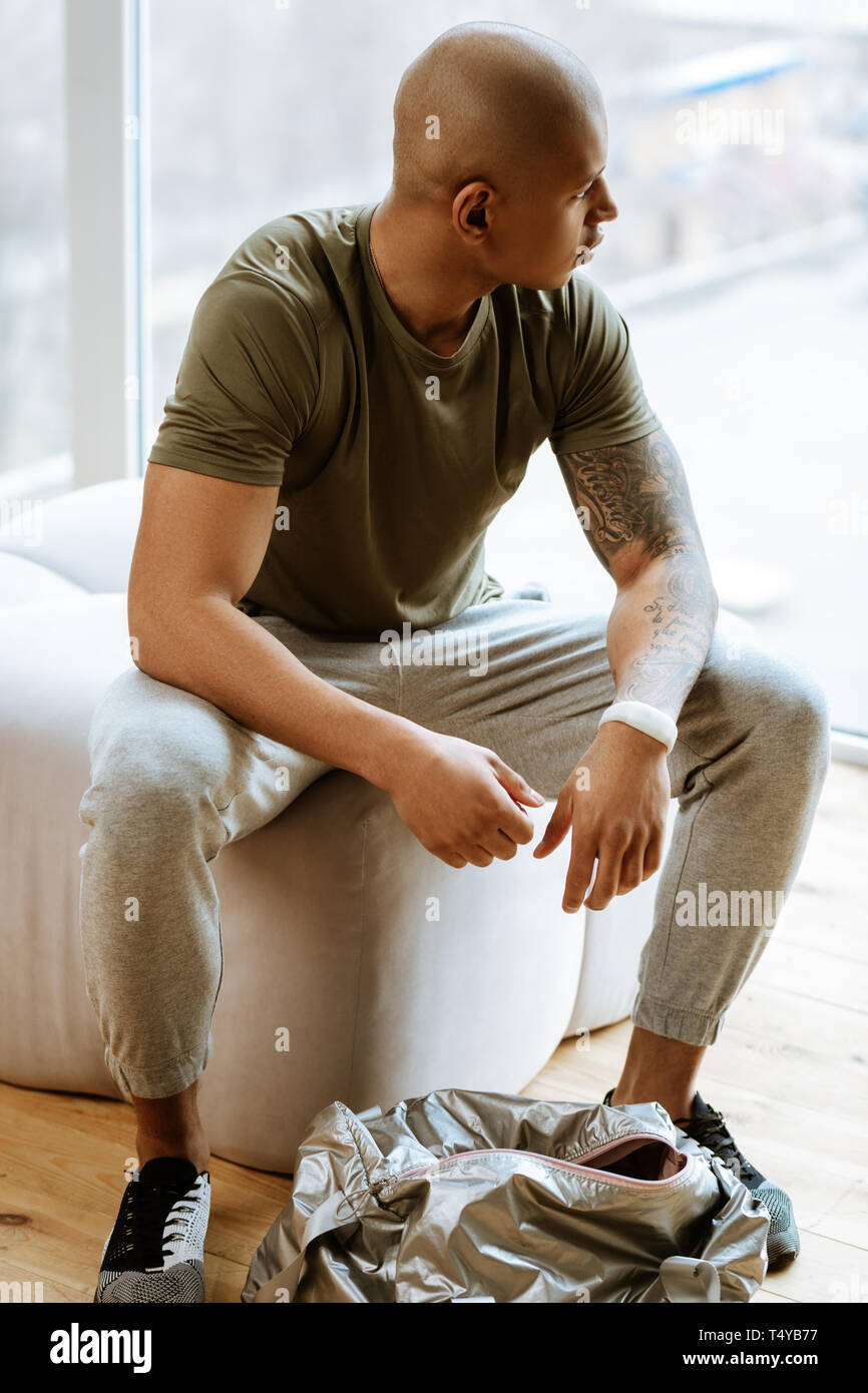 Bodybuilder sitting on sofa at home near big bag with sport items Stock ...