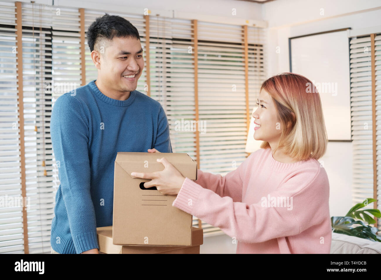 Happy asian couple carry cardboard boxes while moving to new house in ...
