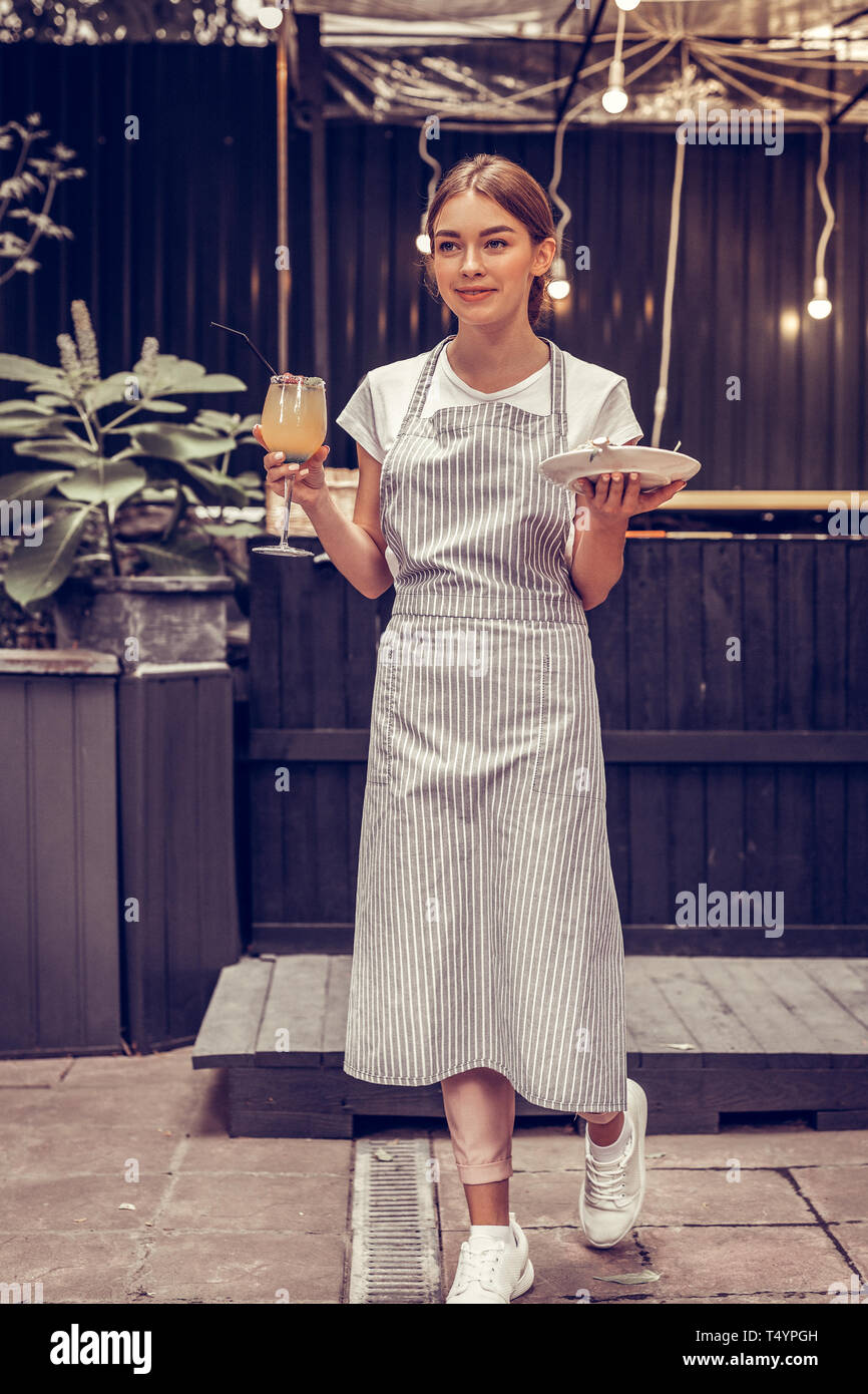 Delighted young woman brining food to the guests Stock Photo - Alamy