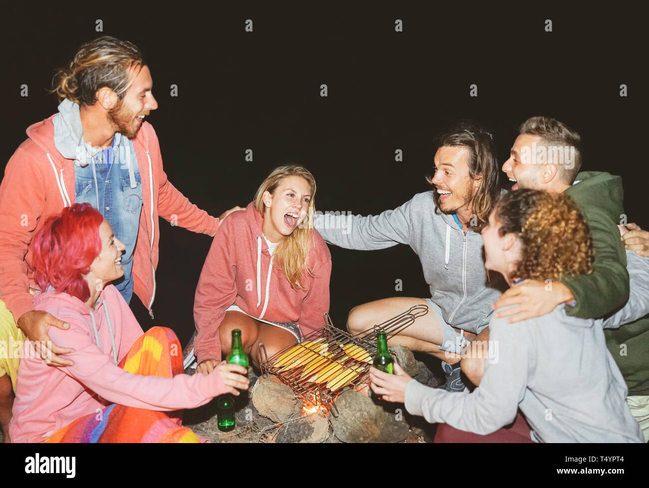 Happy friends camping together and cooking corn at night outdoor ...