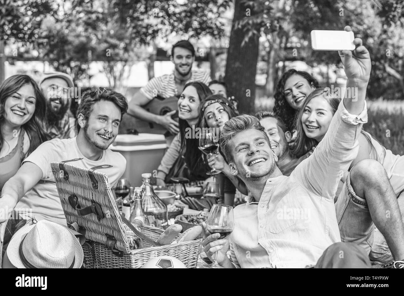Group of friends making a picnic barbecue and taking selfie with mobile smartphone in park ...