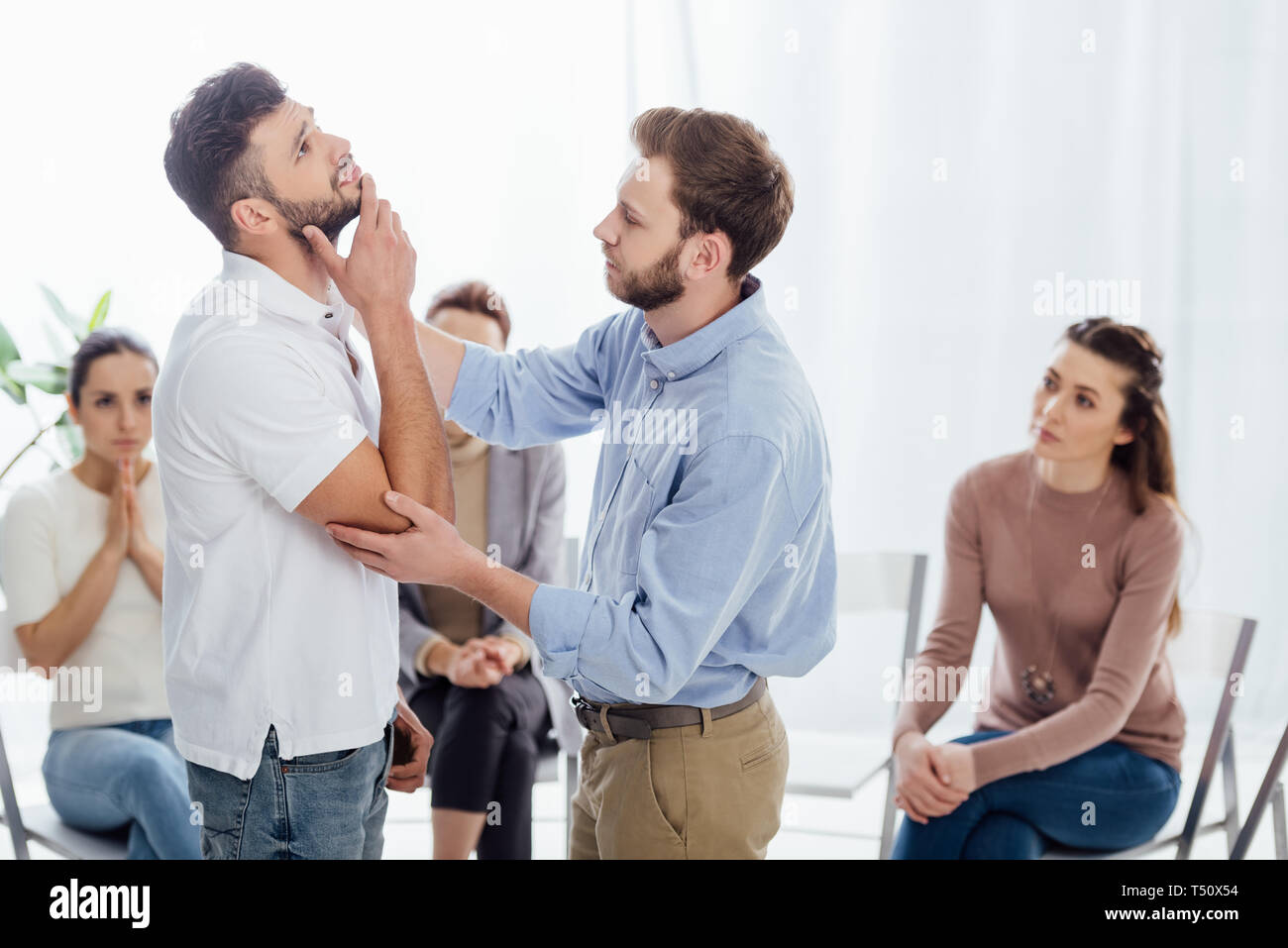 man consoling another man while people sitting on chairs during group ...