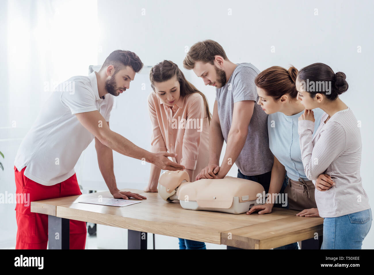 group of people with handsome instructor performing cpr on dummy during ...