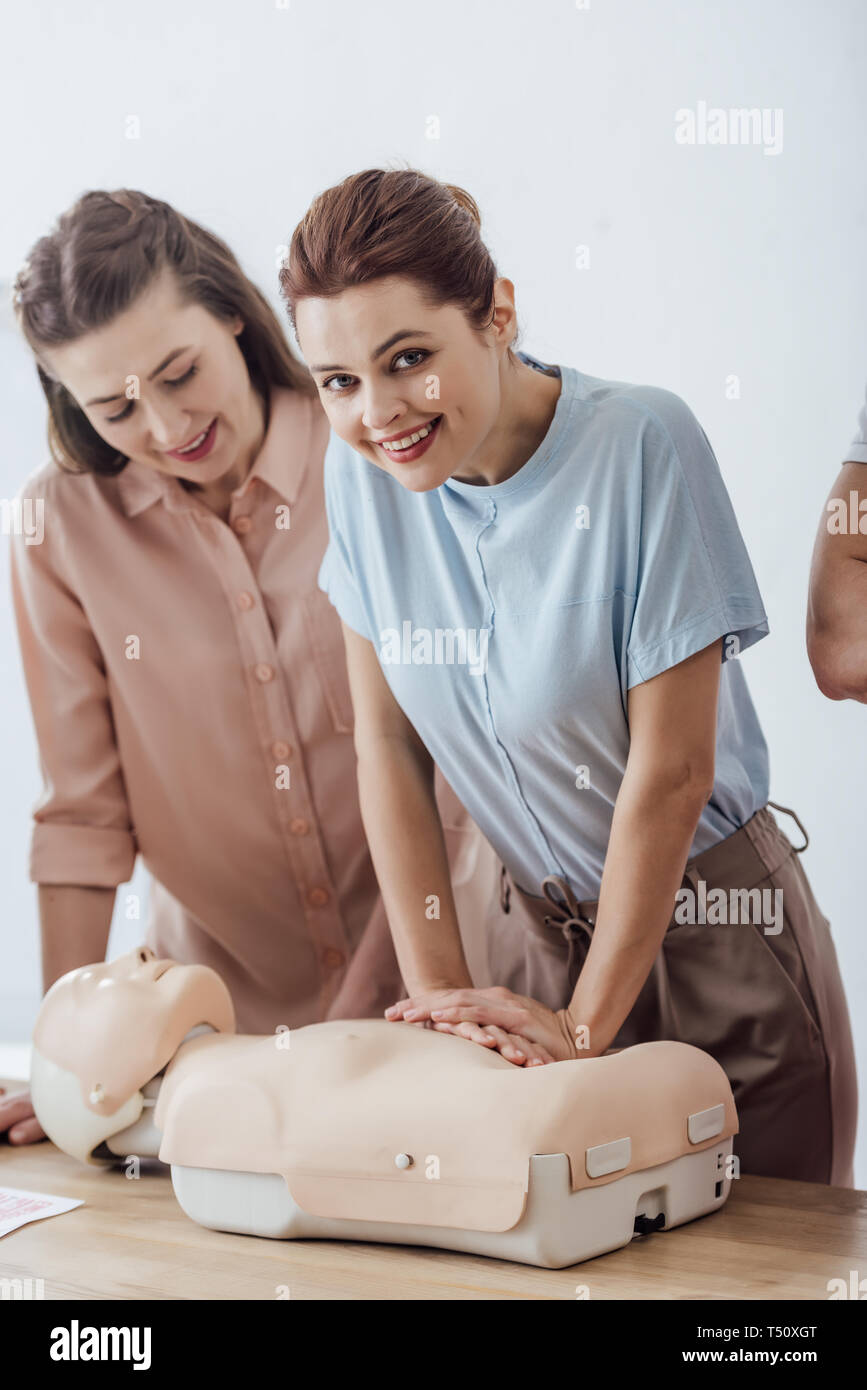 smiling woman performing chest compression on dummy and looking at ...