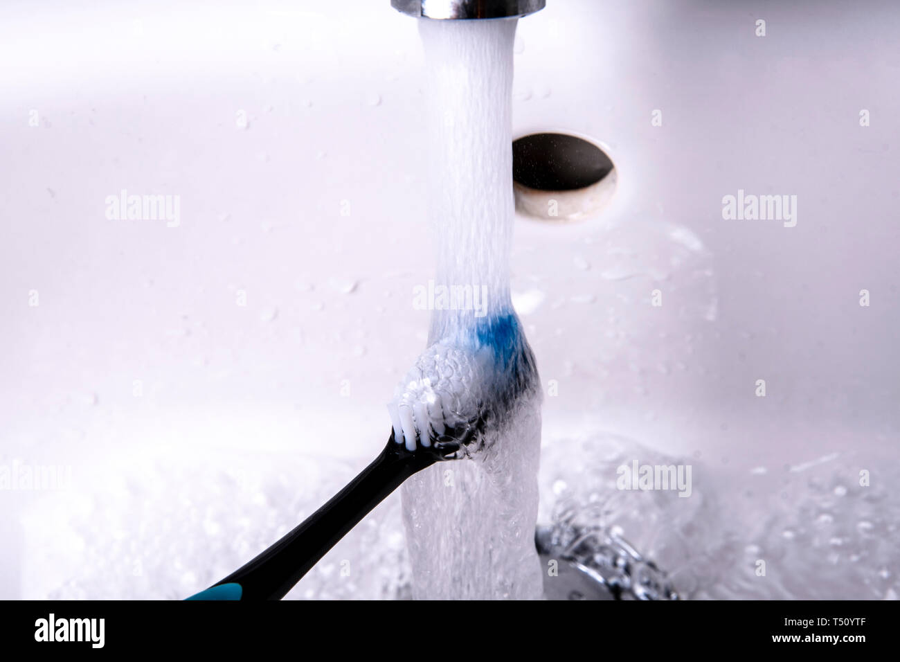 Toothbrush is cleaned in the sink under running water Stock Photo - Alamy