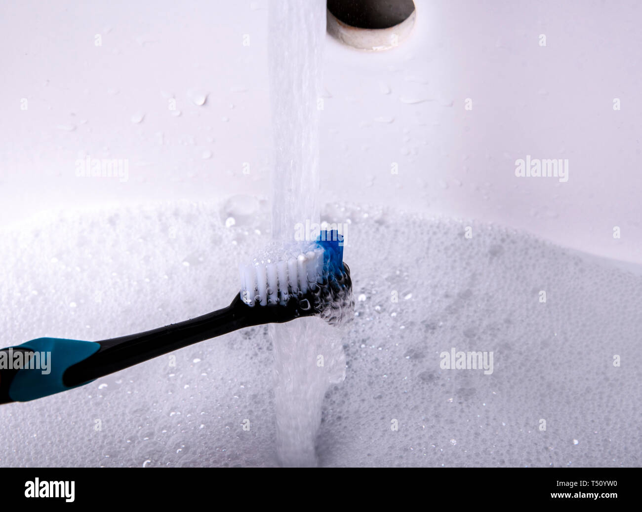 Toothbrush is cleaned in the sink under running water Stock Photo - Alamy