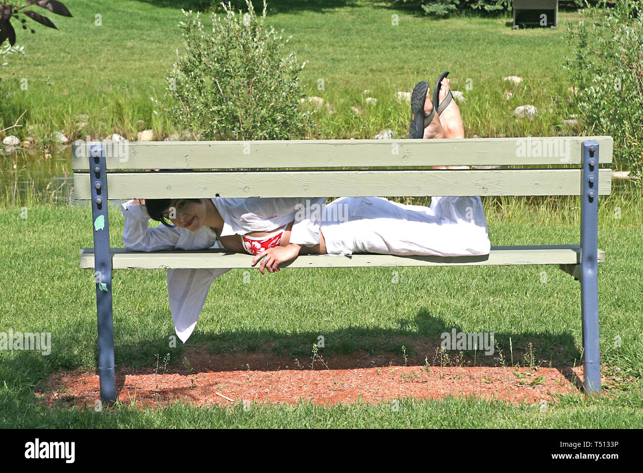 Pretty dark haired woman lying on a wooden park bench Stock Photo - Alamy