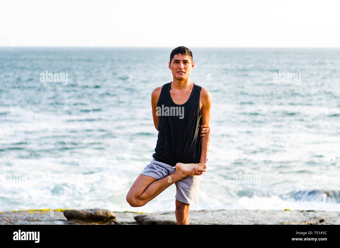 Young man practice yoga on the beach with a clear blue sky background ...
