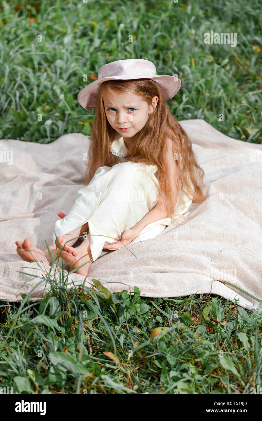 Little girl in a white dress and hat in garden. A crying child is ...