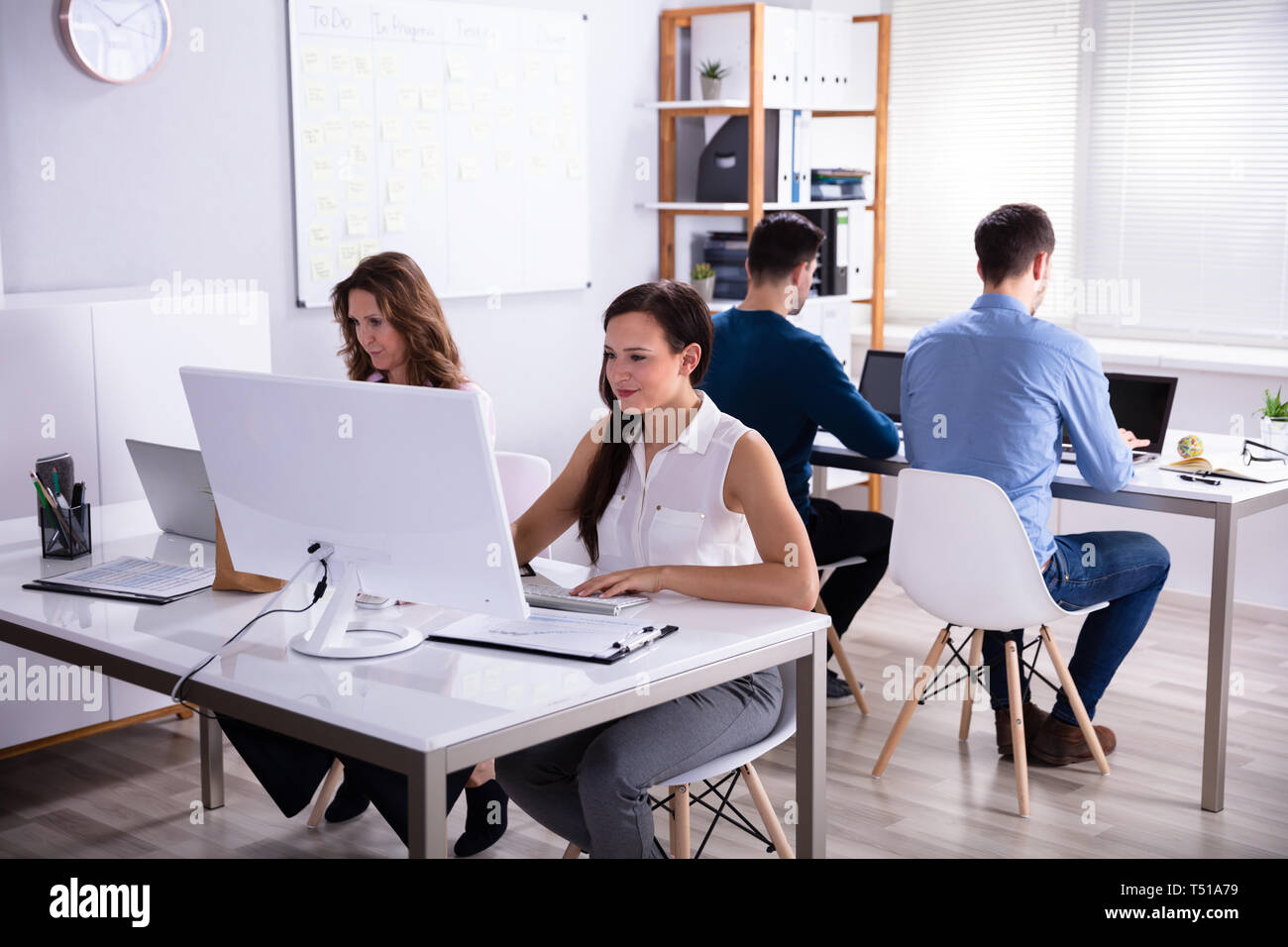 Smiling Young Businesspeople Using Electronic Devices At Workplace In ...