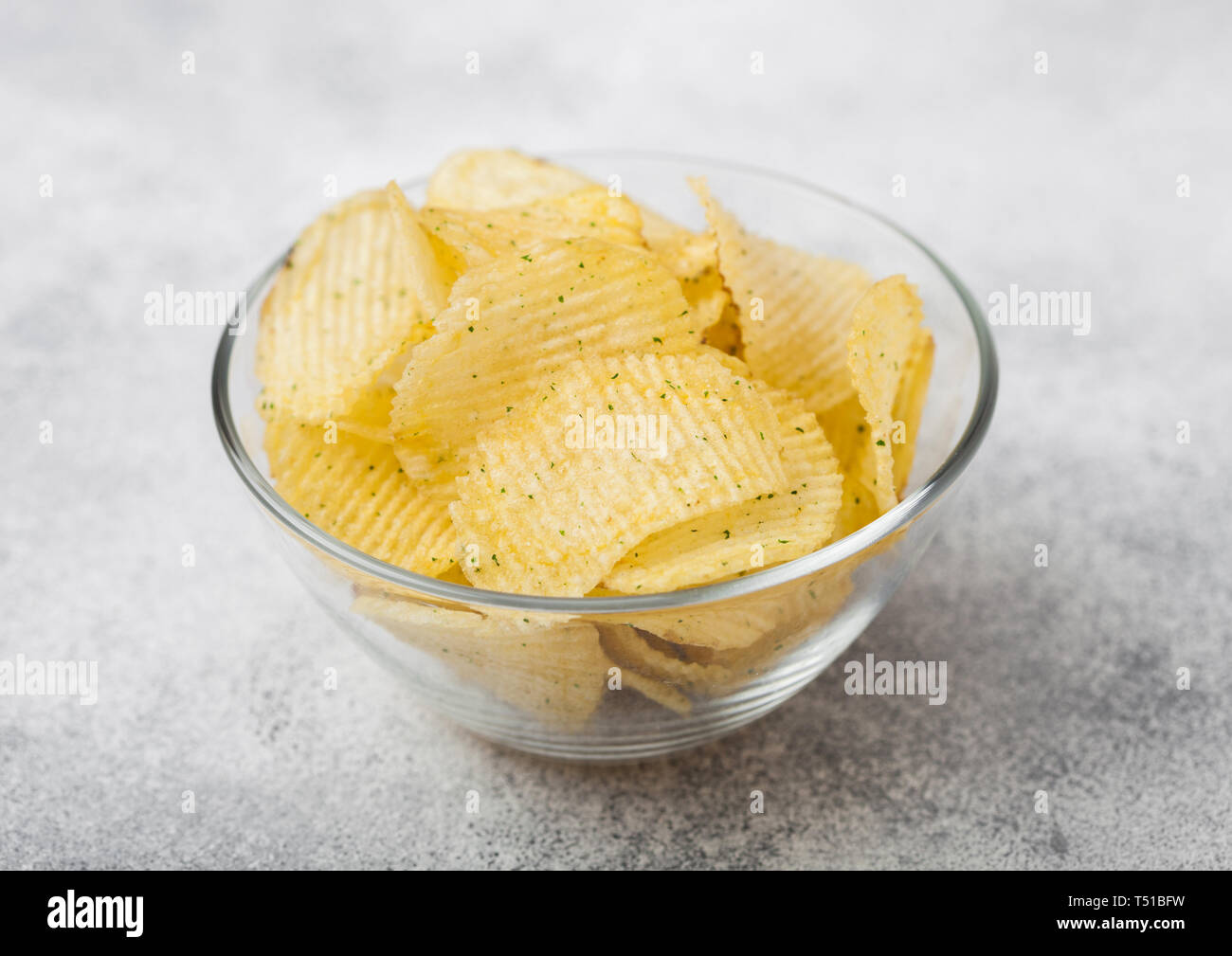 Fresh organic homemade potato crisps chips in glass bowl on light table ...