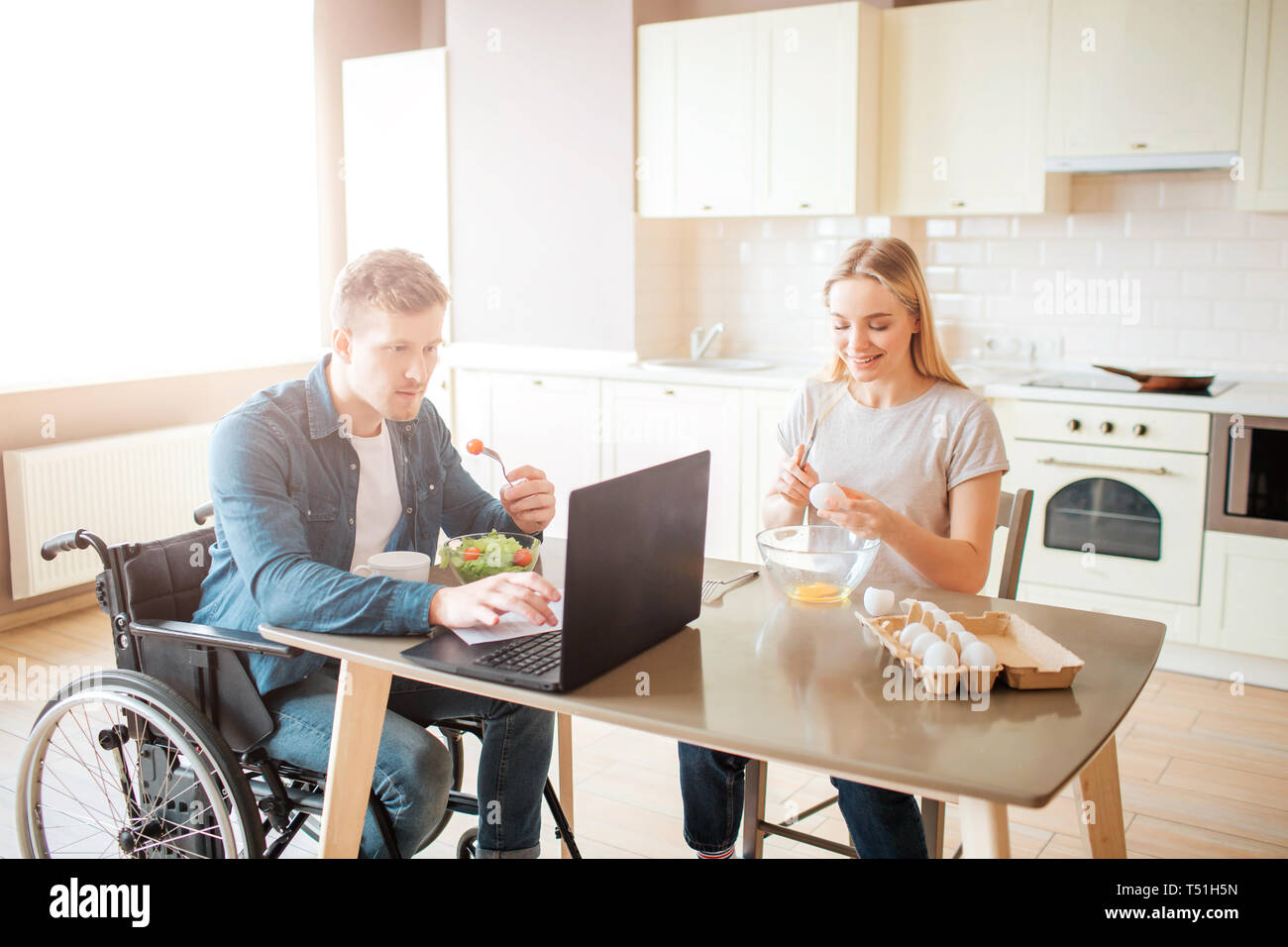 Concentrated young man on wheelchair working with laptop and eating ...