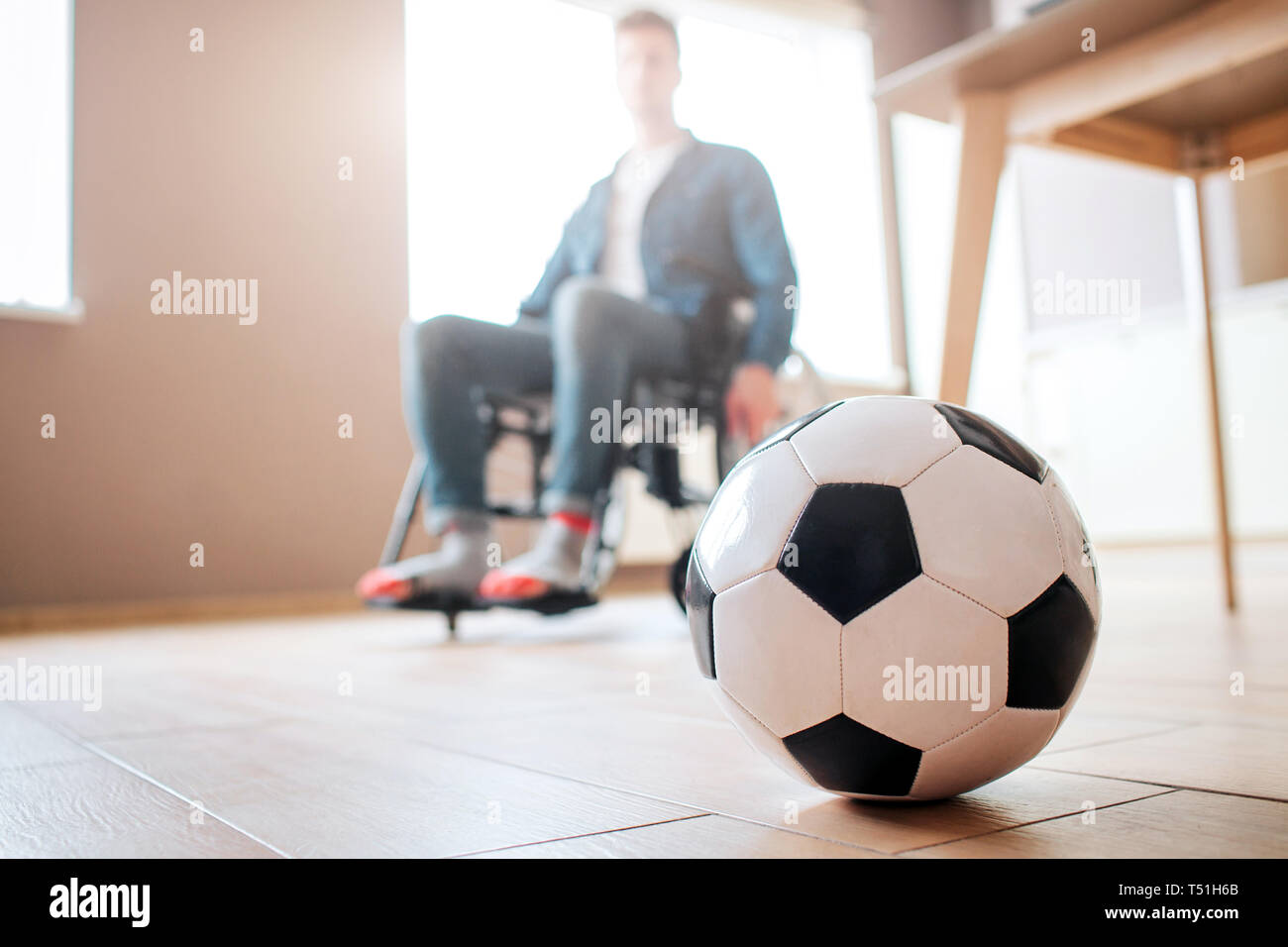 Young man with disability sitting on wheelchair and look down at ball ...