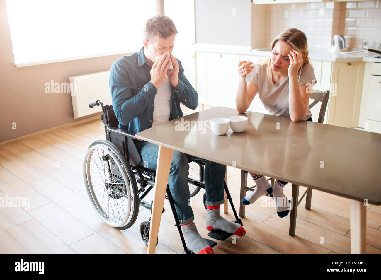 Sick young man with inclusiveness sneezing with healthy woman at table ...