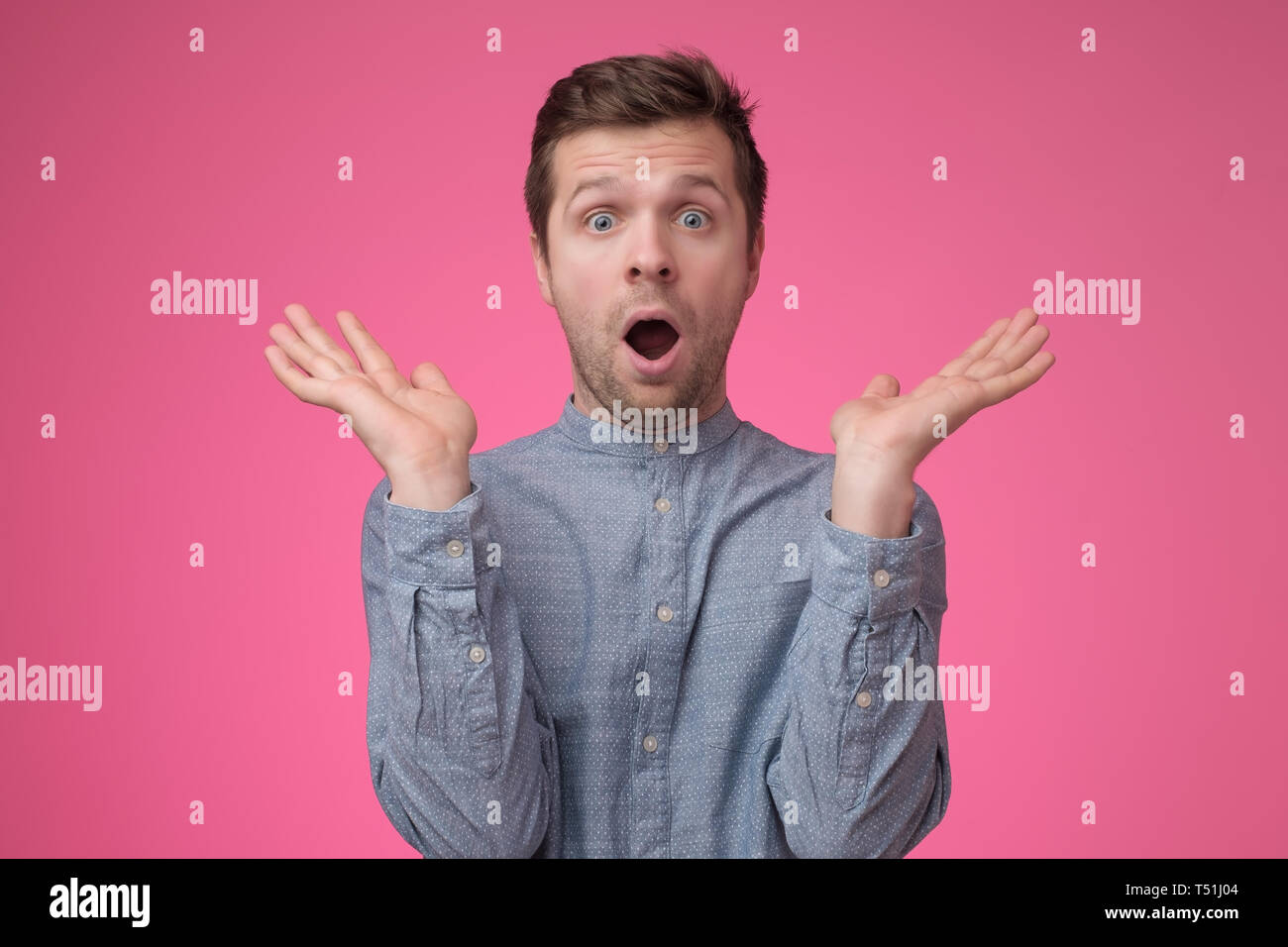 Shocked face of caucasian man in blue shirt on pink background Stock ...