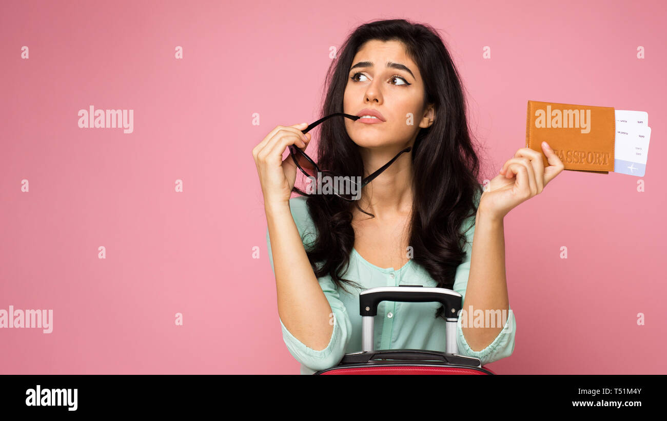 Confused woman holding passport with tickets, pink background Stock ...