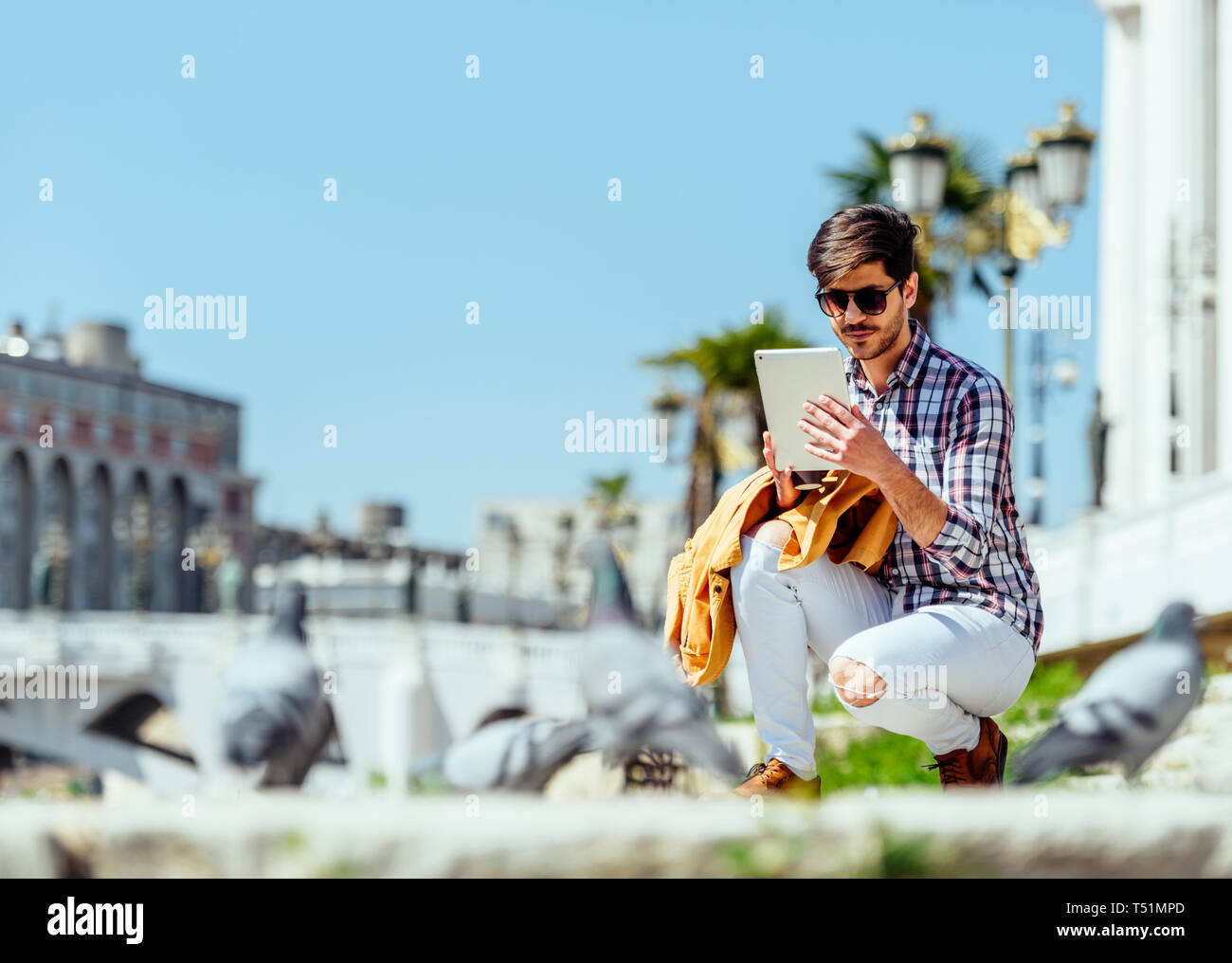 Modern businessman looking at his tablet while sitting on the ground at ...