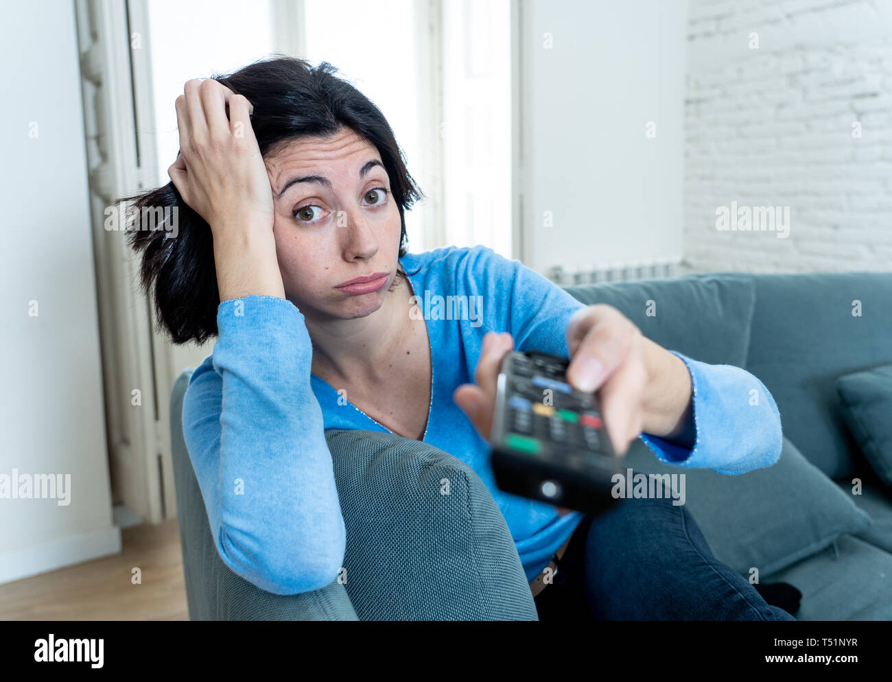 Young upset woman on sofa using control remote zapping bored of bad TV ...
