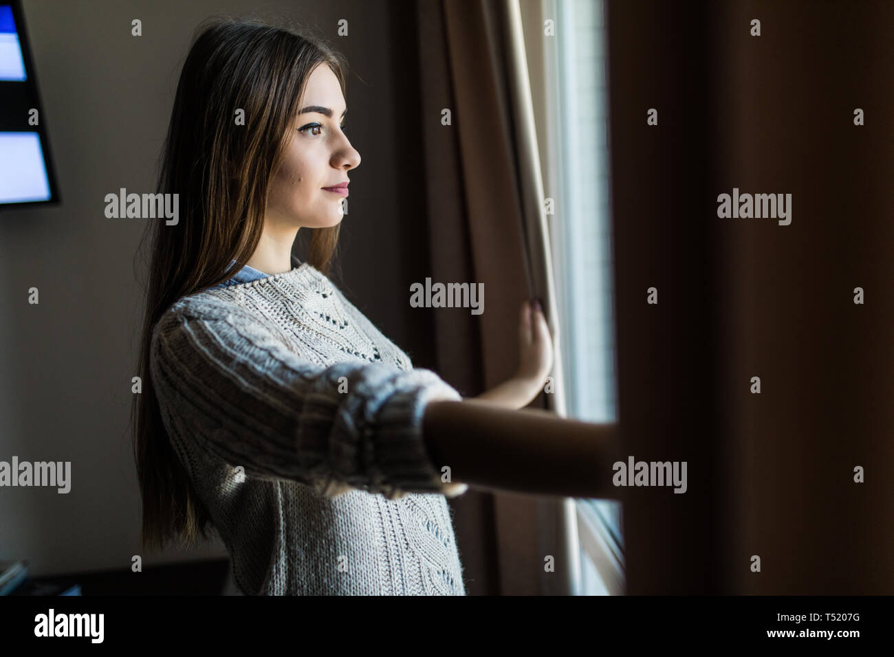Beautiful woman opening curtains and looking through the window Stock ...