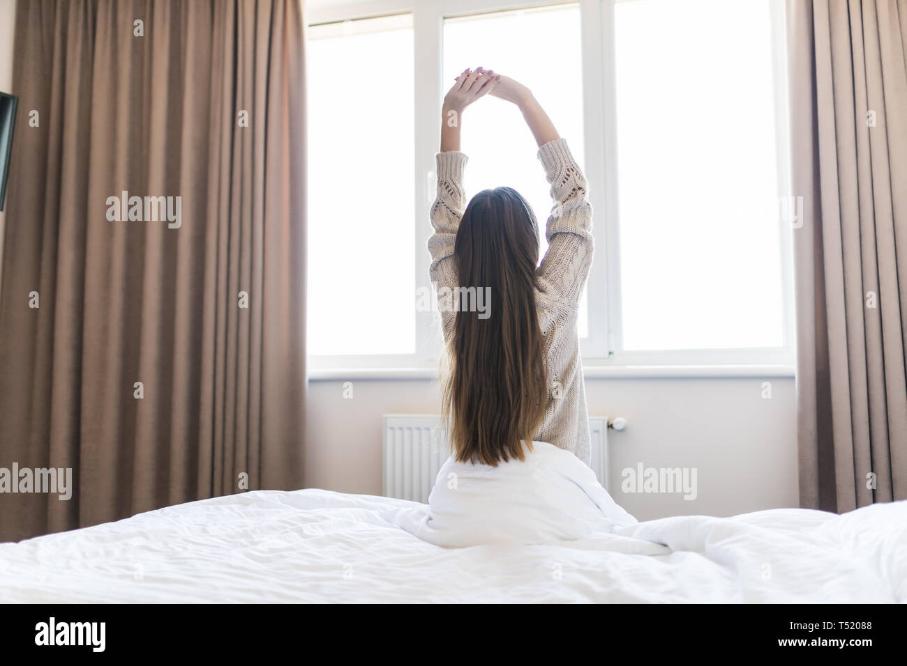 Rear view of woman stretching in bed after wake up in morning with ...