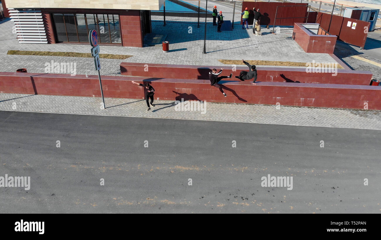 Three athletic young men overcoming obstacles and running on the road ...