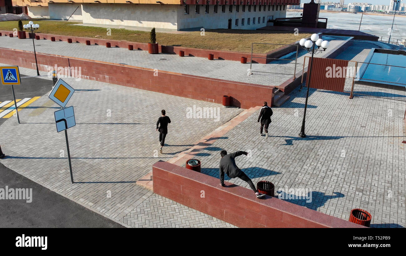 Three young men overcoming obstacles and running on the streets. Aerial ...