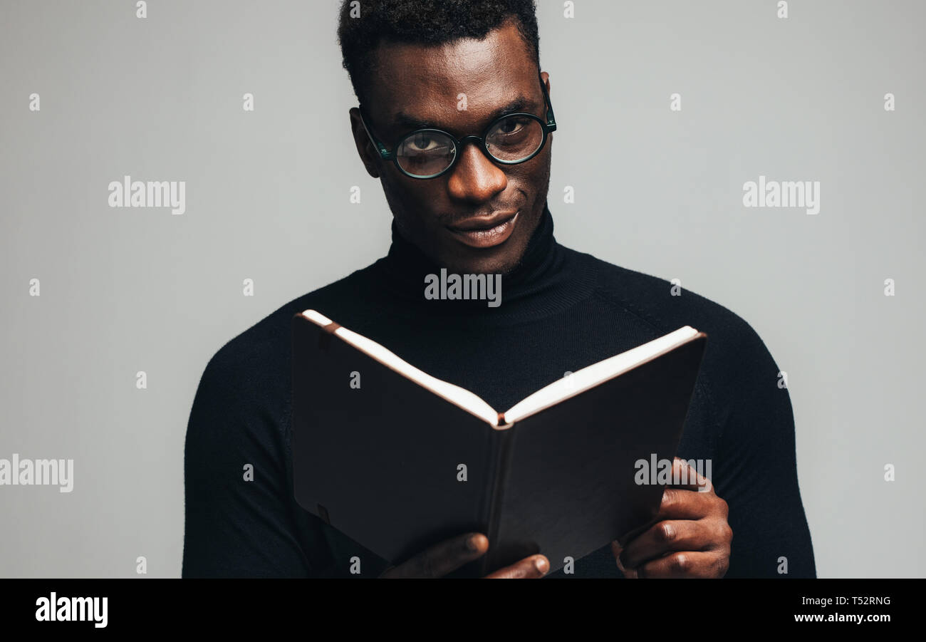 African man looking at camera with a book in hand. Young guy reading a ...