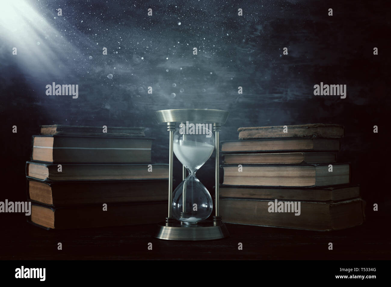 Hourglass as time passing concept and old books in front of black wall ...