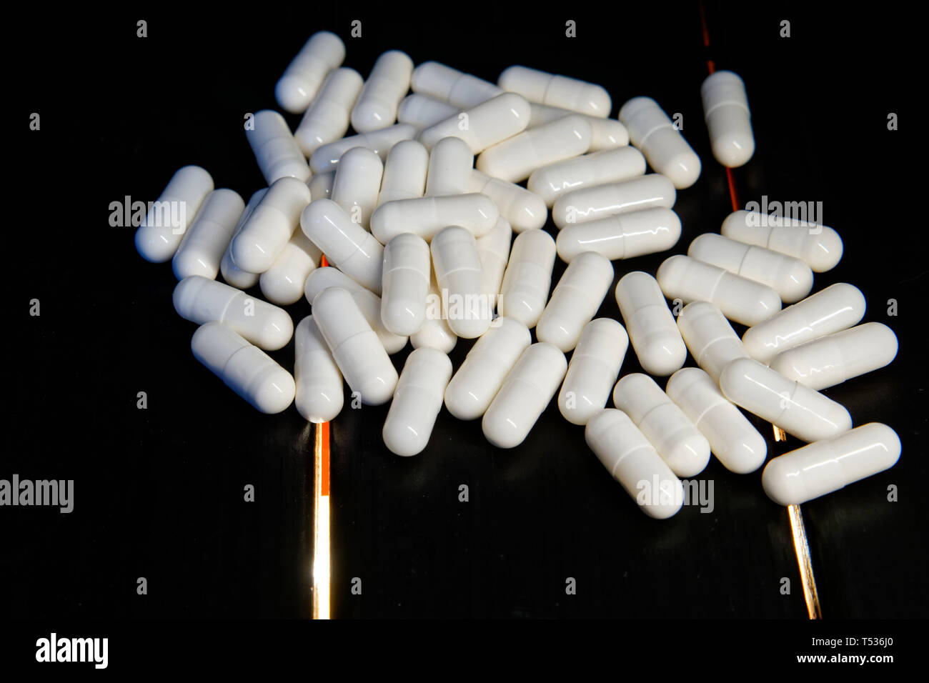 White capsule pills on a black wooden background with LED light ...