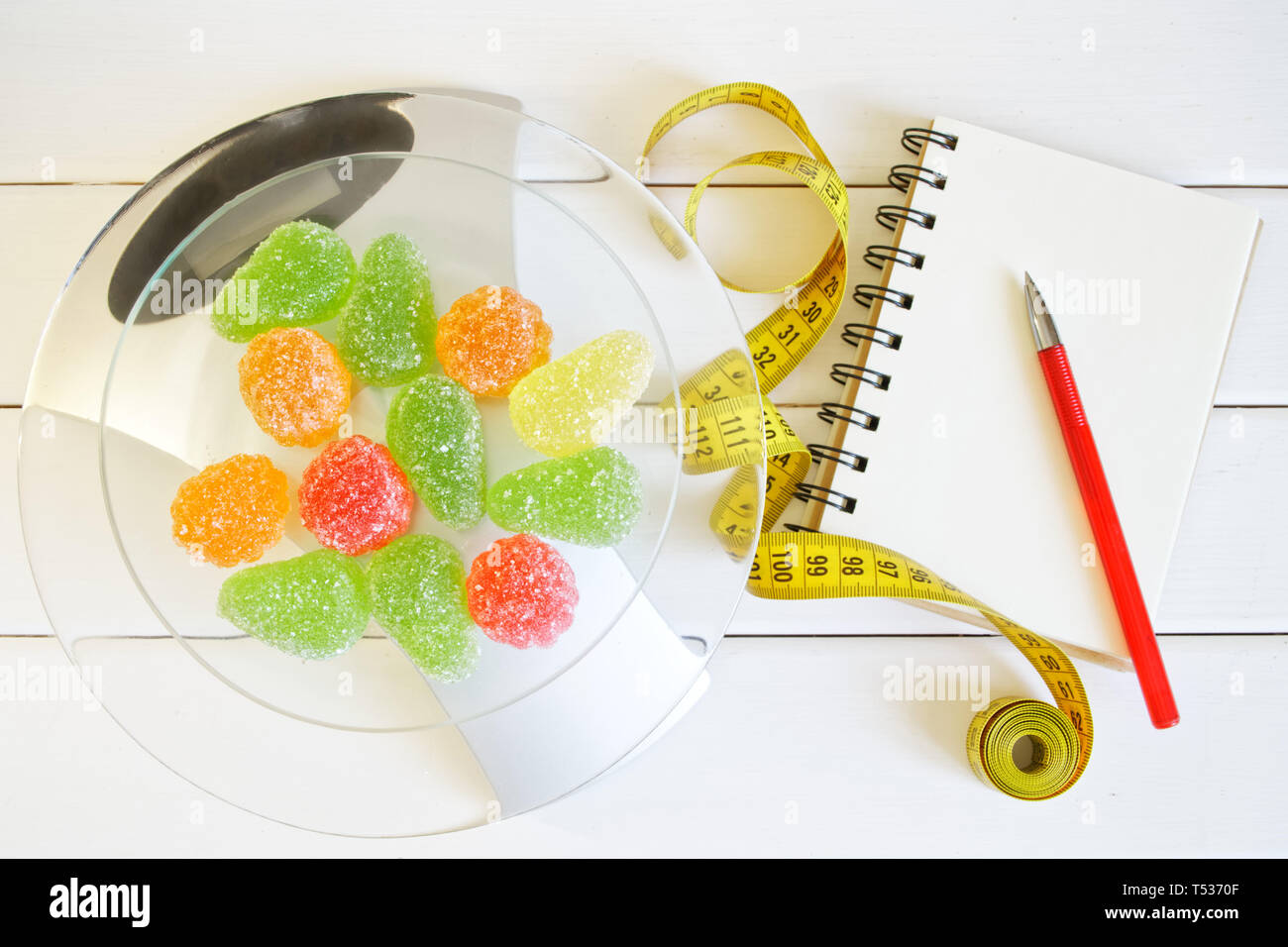 Fruit jelly on kitchen scales next to a notebook, a pen and a tape ...
