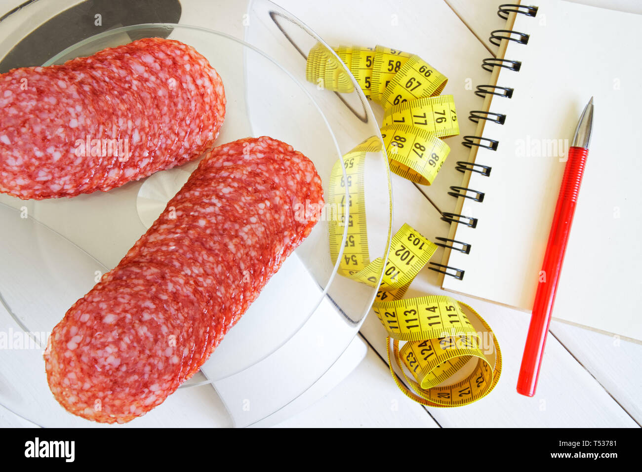 Sliced raw smoked sausage on kitchen scales, next to a notebook, a ...